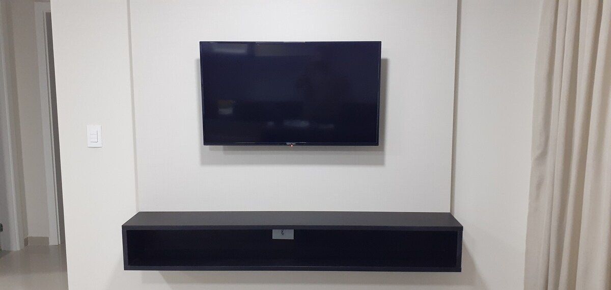 Televisão de tela plana fixada em uma parede sobre um rack de entretenimento preto.