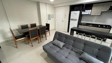 Espaço compacto com sofá, mesa de jantar, cadeiras, área de cozinha e uma porta.