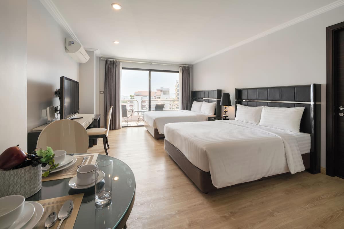 Quarto de hotel com duas camas, área de refeições e varanda com vista para a cidade.