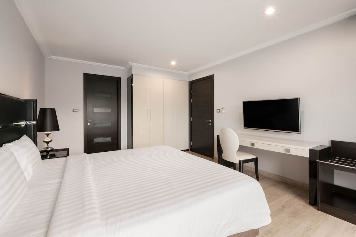 Quarto de hotel moderno com uma cama grande, uma escrivaninha, uma cadeira, uma televisão e um guarda-roupa.