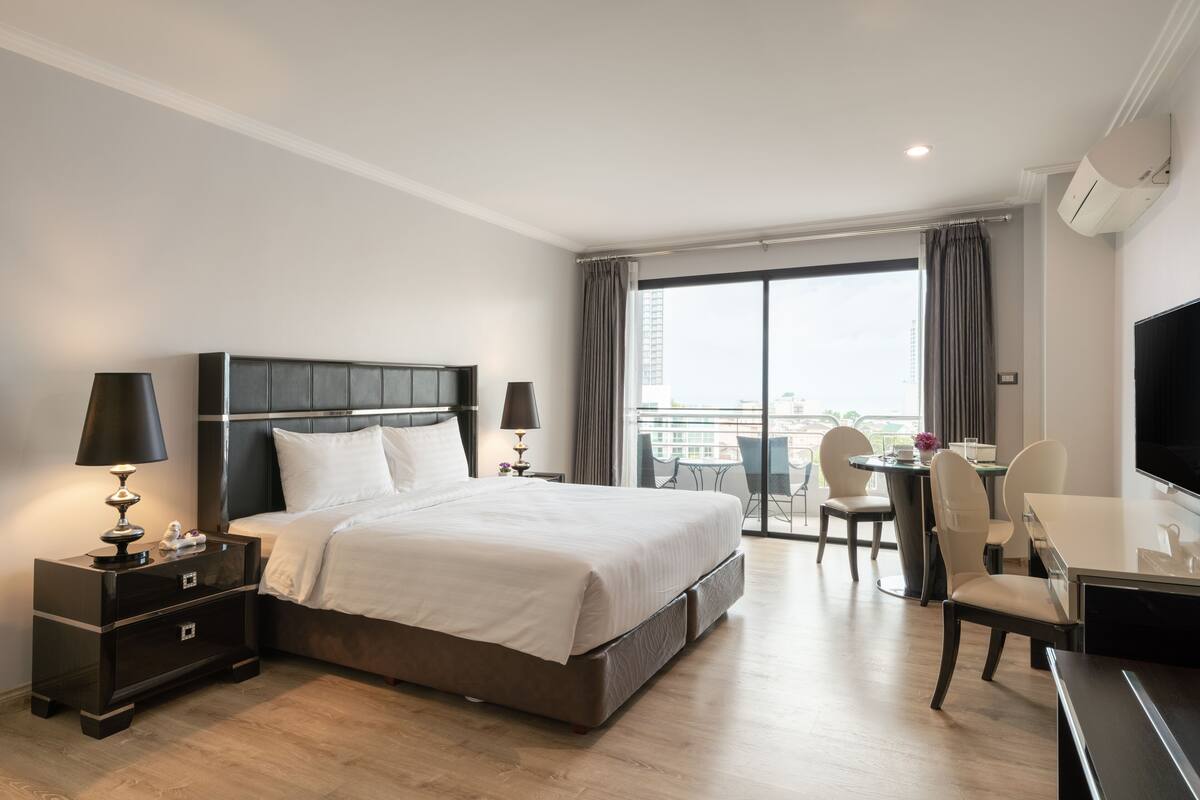Quarto de hotel com cama grande, escrivaninha, cadeira e varanda com vista.