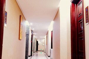 Corredor de hotel com portas em ambos os lados, piso ladrilhado e escada no centro.