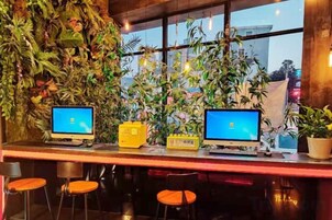 Zona de bar com dois computadores, uma planta em vaso e vista pela janela.