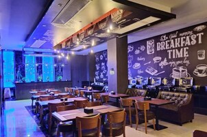 Um restaurante com mesas, cadeiras, um balcão e uma parede decorada com ilustrações sobre o café da manhã.
