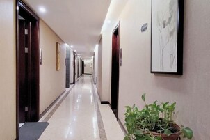 Corredor de hotel com portas em ambos os lados, um vaso de planta e quadros nas paredes.