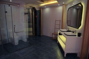 Uma casa de banho moderna com cabine de duche em vidro, lavatório branco com espelho e chão em mosaico.