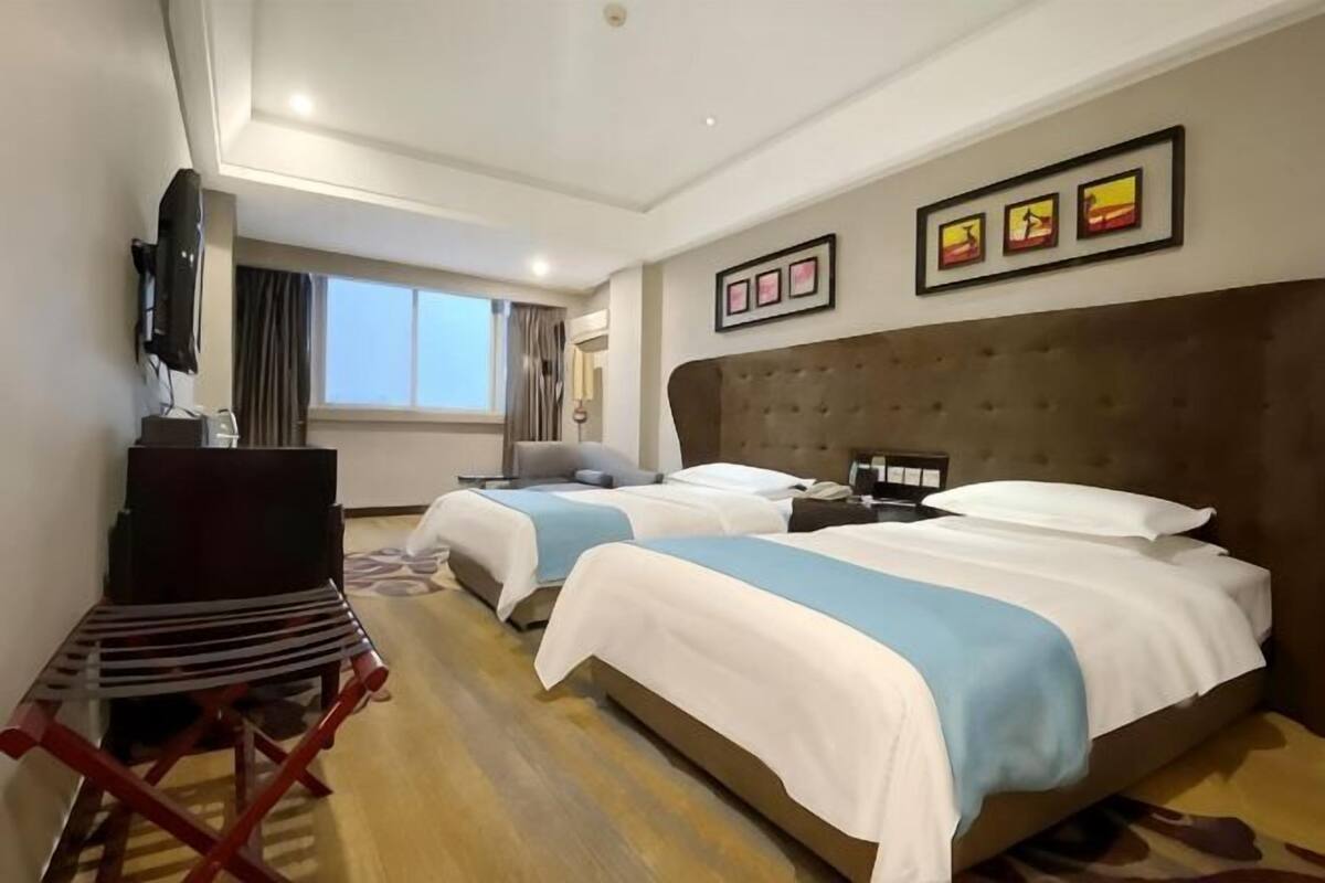 Quarto de hotel com duas camas, televisão, escrivaninha e janela.
