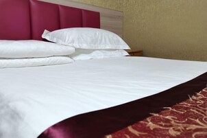 Uma cama com roupa de cama branca e cabeceira vermelha.
