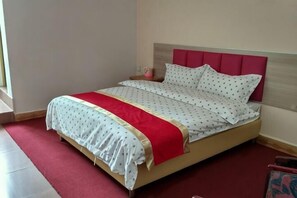 Uma cama com colcha vermelha e branca, cabeceira de madeira e mesa de cabeceira com abajur.