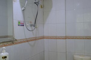 Casa de banho com azulejos brancos, chuveiro, sanita e dispensador de sabonete.
