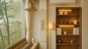 Quarto com prateleira de madeira, luminária de chão e janela com vista para árvores.