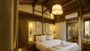 Quarto de hotel com teto de madeira, cama com roupa de cama branca, luminárias fixadas na parede e janela com cortinas.