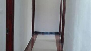 Um corredor com uma porta de madeira à esquerda e uma parede branca à direita.
