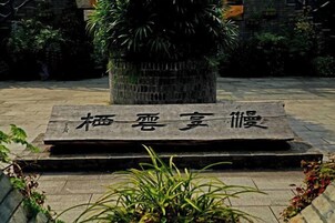 Uma placa de pedra com caracteres chineses em um pátio com uma planta em vaso e paredes de pedra.