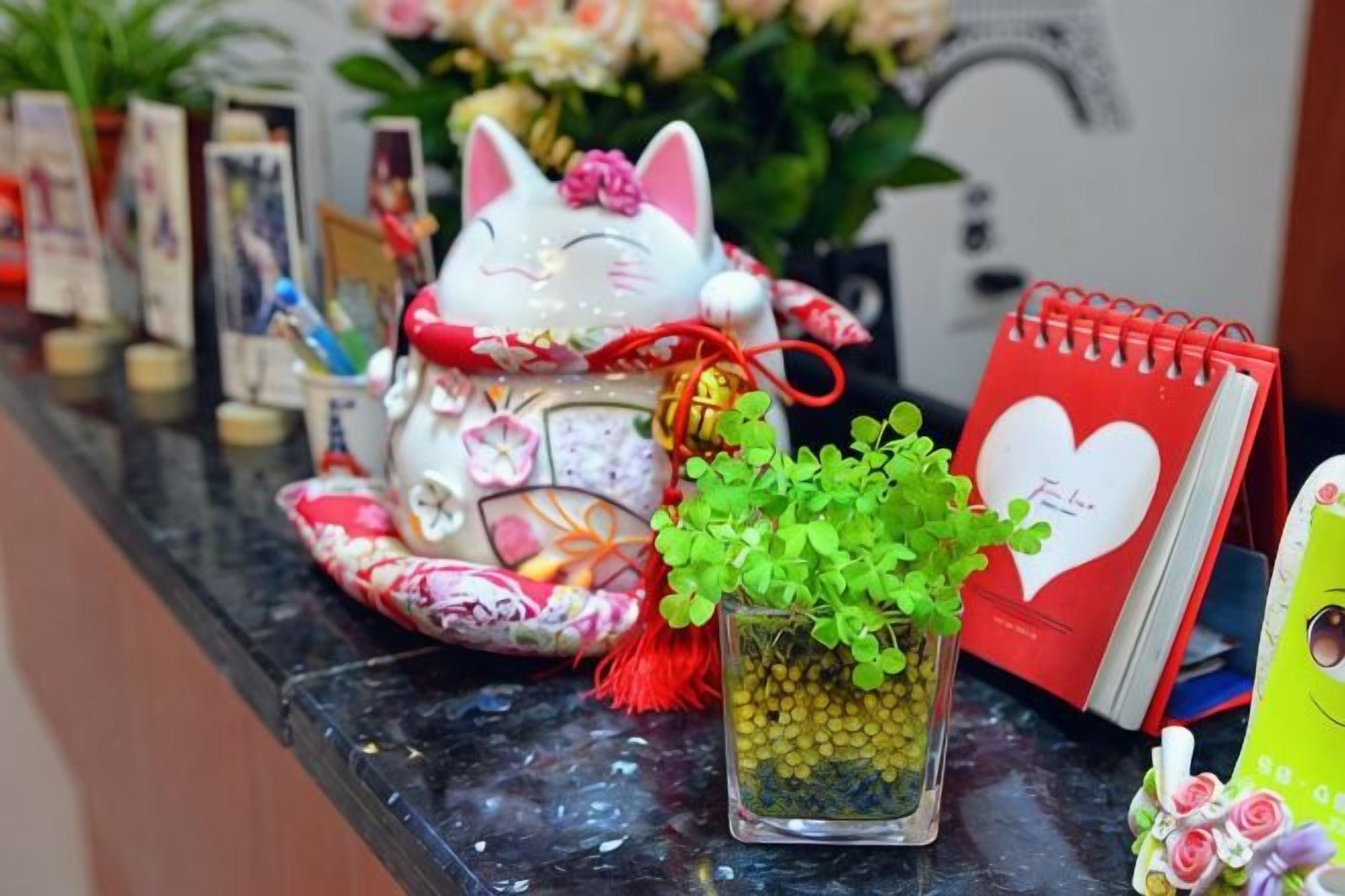 Um balcão com uma estatueta de gato decorativa, uma pequena planta em vaso, um caderno vermelho com um coração e um calendário.