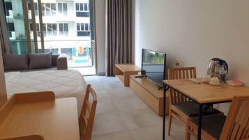 Quarto de hotel com cama, escrivaninha com televisão, máquina de café e vista para a varanda.