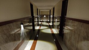 Um corredor com piso espelhado, paredes com acabamento que imita mármore e portas ao longo das laterais.
