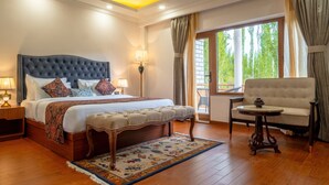 Quarto de hotel com uma cama grande, uma mesa de cabeceira com luminária, uma pequena mesa redonda e um sofá.
