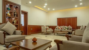 Uma sala de estar ampla com um aparador de madeira exibindo objetos decorativos, dois sofás com almofadas coloridas e uma mesa de centro de madeira.
