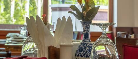 Uma mesa de jantar com um vaso de flores, uma toalha branca, um jarro de vidro e uma colher.