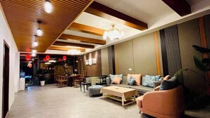 Uma sala de estar moderna com sofá, banqueta e mesa de centro. Há uma área de jantar com cadeiras e uma mesa ao fundo.