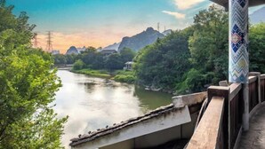 Vista para o rio a partir de uma varanda com um pilar trabalhado, o rio, vegetação e montanhas ao longe.