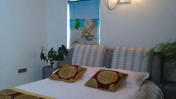 Quarto com cama, almofadas, mesa de cabeceira, planta em vaso, janela com vista para a praia e luminária fixada na parede.
