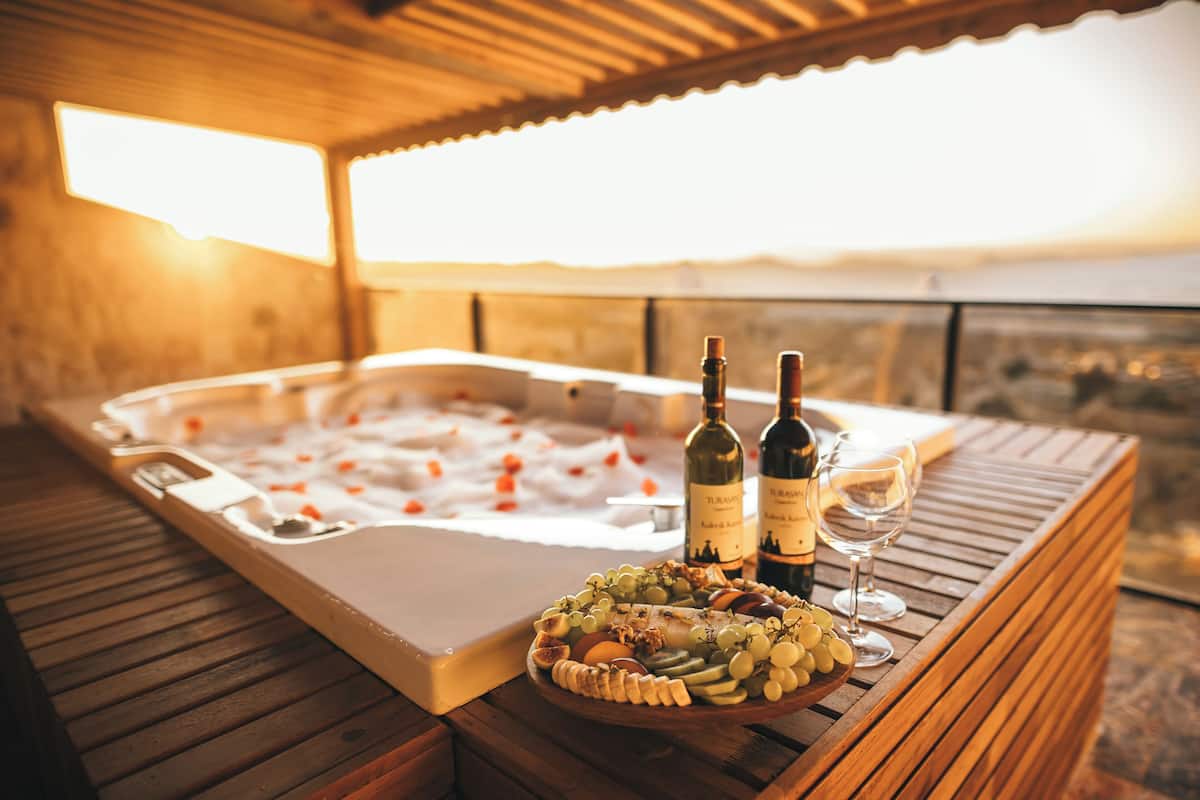 Uma mesa de madeira com uma banheira de hidromassagem, uma garrafa de vinho, uma taça de vinho e um prato de frutas.