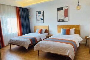 Quarto de hotel com duas camas, cabeceiras de madeira e uma grande janela com cortinas.