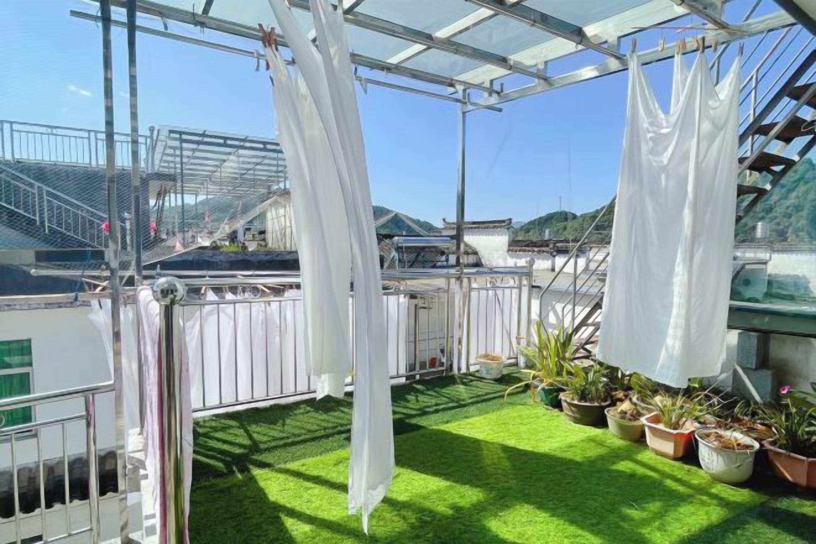 Jardim no terraço com vasos de plantas, uma estrutura de estufa de vidro e uma cortina branca.