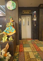 Um saguão de hotel com um relógio, uma estátua, uma placa indicando o Restaurante Rooftop, um elevador e um piso com padrão.