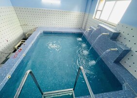 Piscina com uma escada para acesso, rodeada por paredes azulejadas e uma janela.