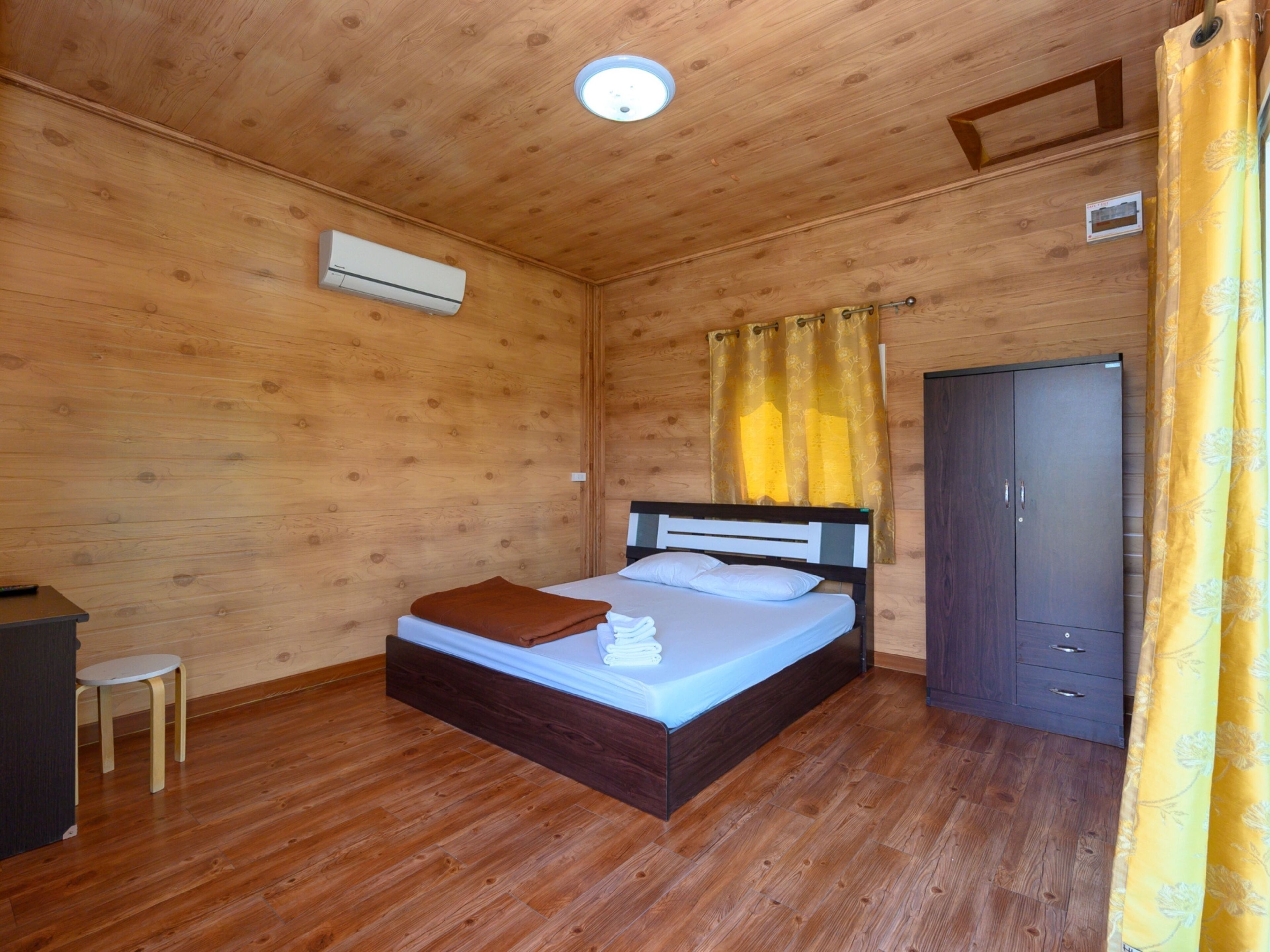 Quarto com painéis de madeira, uma cama, uma mesinha e um guarda-roupa.