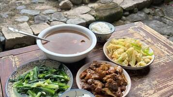 Uma mesa de madeira com diversos pratos, incluindo uma tigela de sopa, um prato de legumes, uma tigela de arroz e um prato com carne.