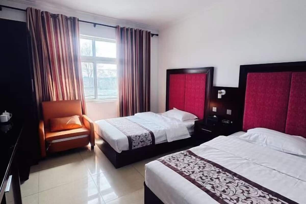 Quarto de hotel com duas camas, uma cadeira, uma escrivaninha e uma janela com cortinas.