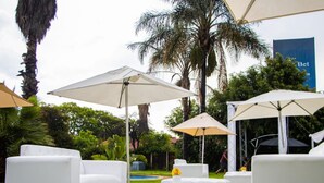 Mobiliário de exterior com guarda-sóis, piscina e palmeiras.