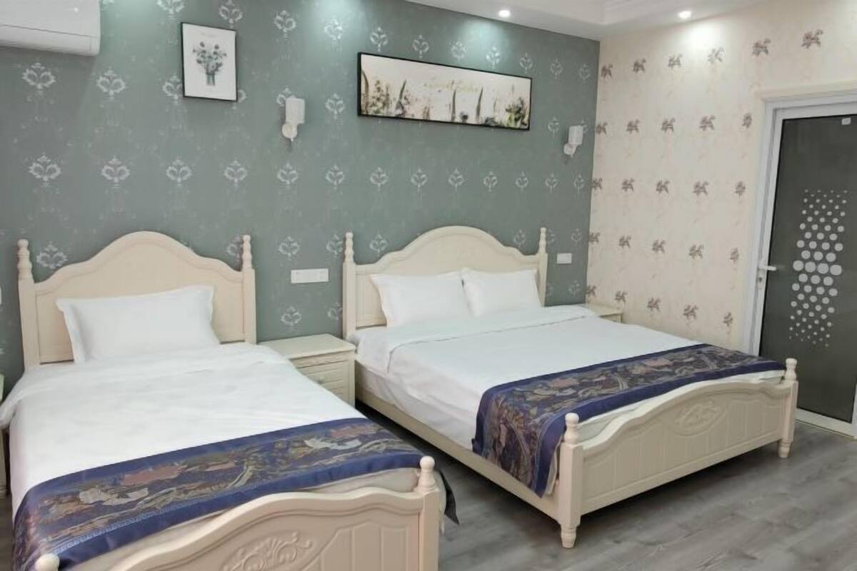 Quarto com duas camas, uma mesinha de cabeceira e uma porta com padrão circular.