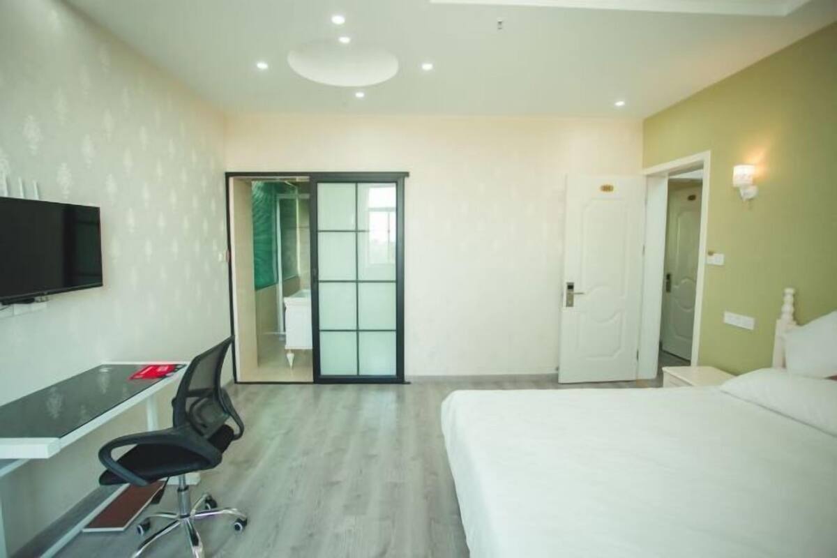 Quarto de hotel com uma cama, uma secretária com cadeira, televisão e uma porta deslizante para uma casa de banho.