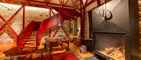 Um interior aconchegante com parede de pedra, vigas de madeira, móveis de couro e lareira.
