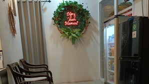 Quarto com um letreiro de neon fixado na parede, geladeira e área de refeições com cadeiras.