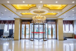 Um saguão de hotel com uma porta giratória, um candelabro e uma grande janela com cortinas.