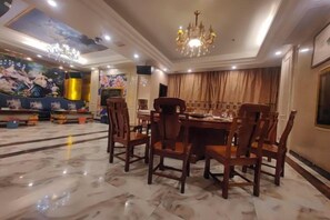 Uma sala de jantar com piso de mármore, cadeiras de madeira, um lustre e uma grande pintura na parede.