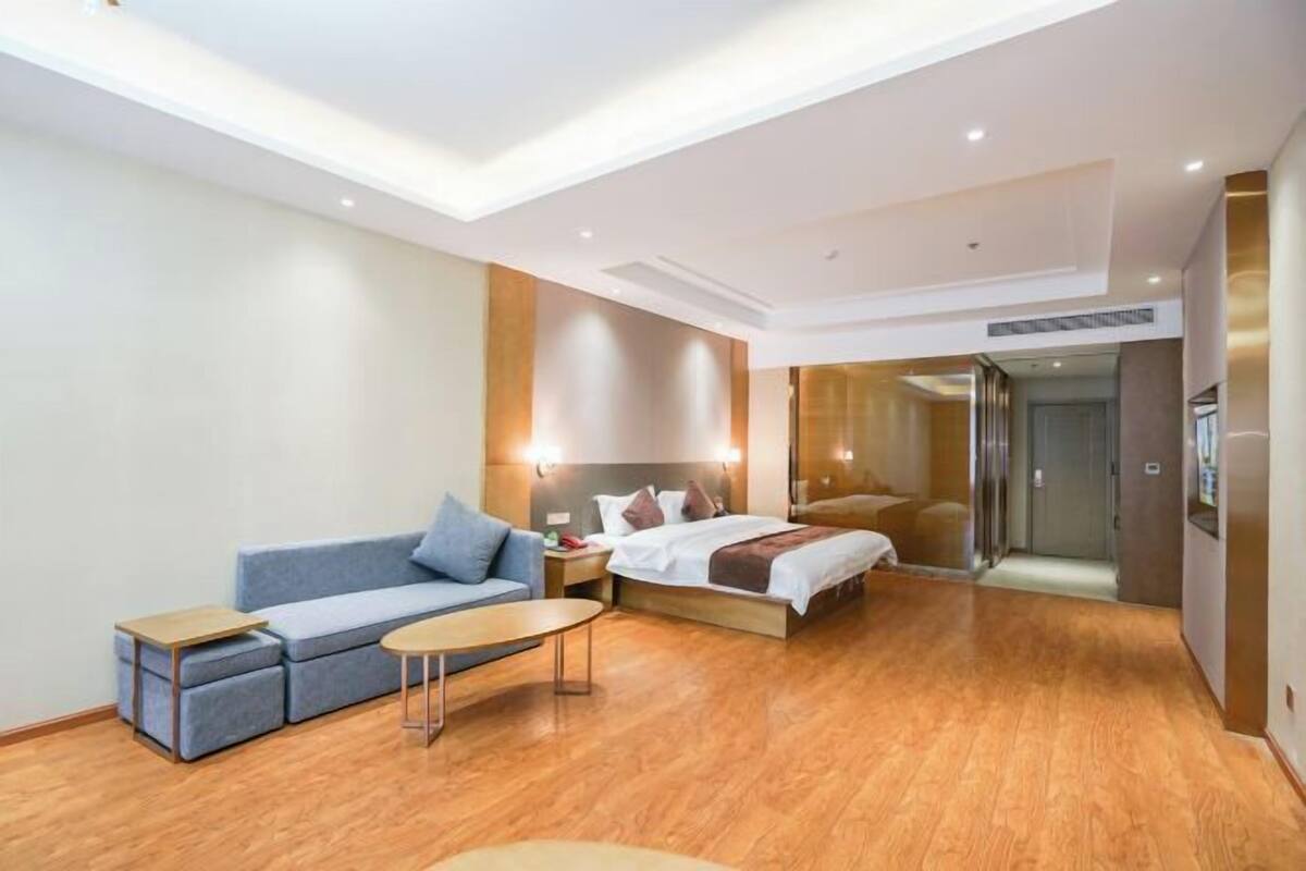 Quarto de hotel moderno com sofá, cama, mesa pequena e espelho.