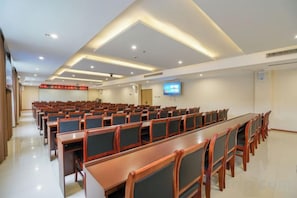 Uma sala de conferências com fileiras de cadeiras e mesas, uma TV de tela plana e uma placa vermelha na parede.