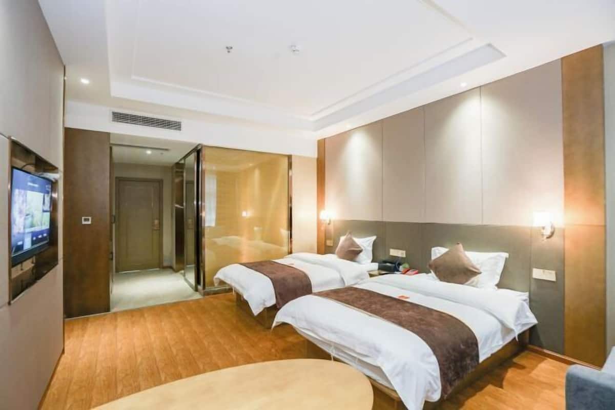 Quarto de hotel com duas camas, televisão, espelho e chão de madeira.