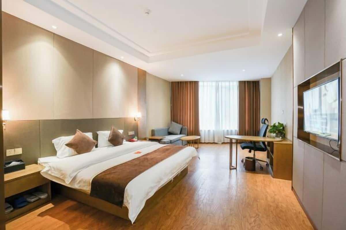 Quarto de hotel com cama, escrivaninha, cadeira e televisão.