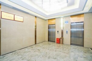 Área moderna de elevadores com piso de mármore, duas elevadoras e uma lixeira vermelha.