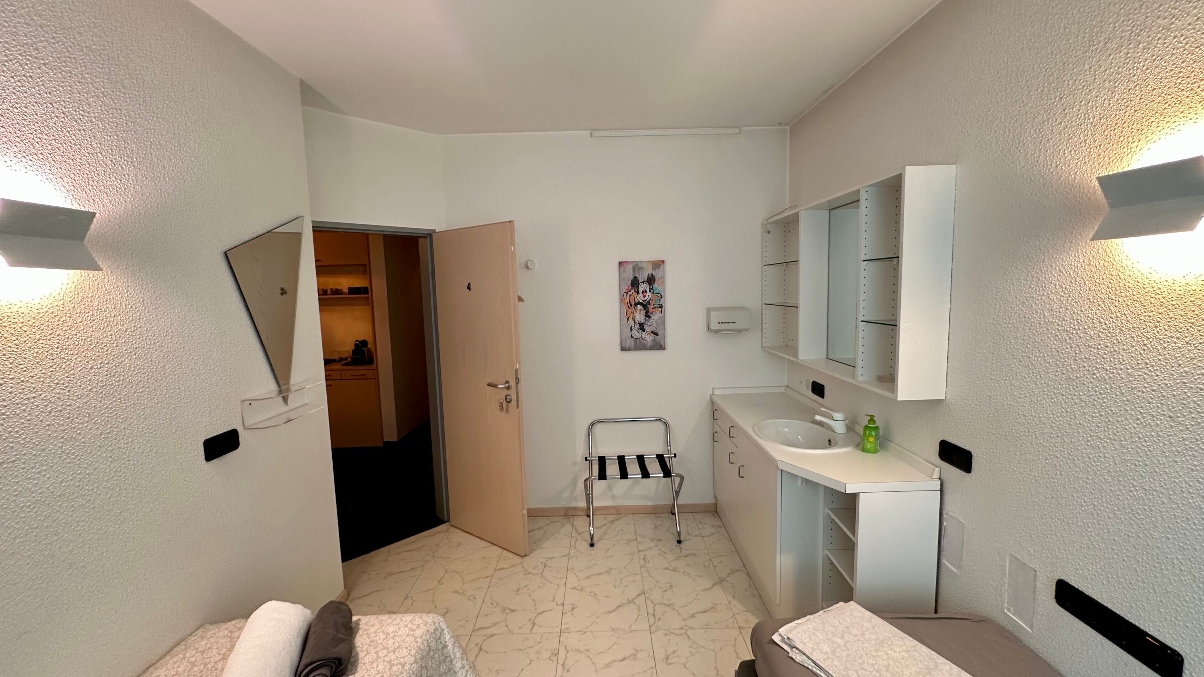 Casa de banho pequena e compacta com lavatório branco, espelho e porta-toalhas.