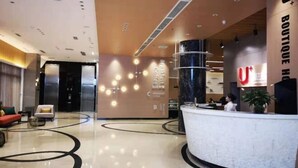 Um lobby de hotel moderno com uma mesa de recepção, o letreiro U+ Boutique Hotel e um grande pilar preto.