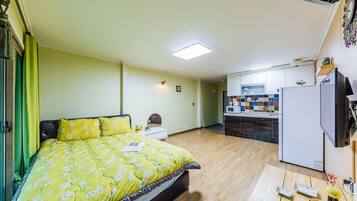 Quarto compacto com cama, mesinha, cozinha compacta e ventoinha no teto.